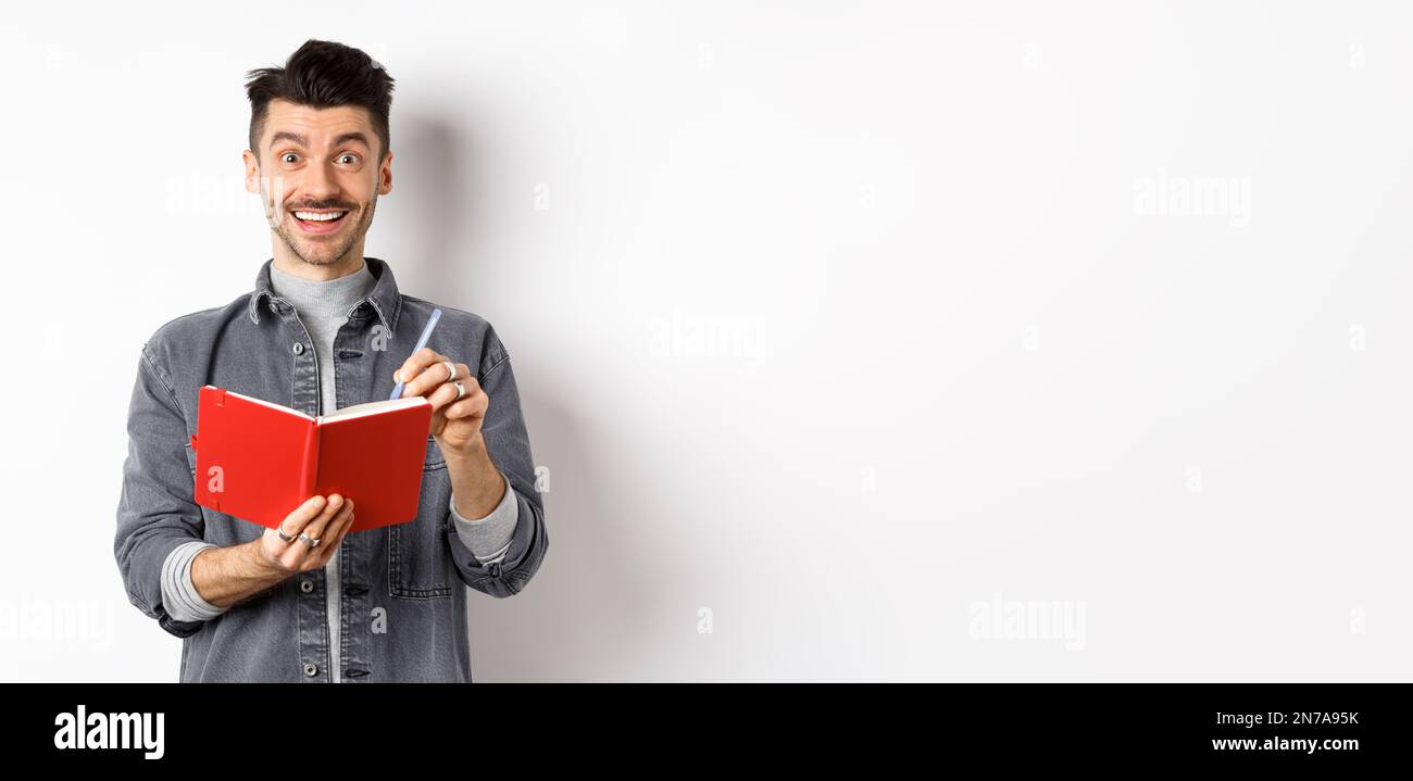 Creative young man smiling excited while taking notes, writing down ...