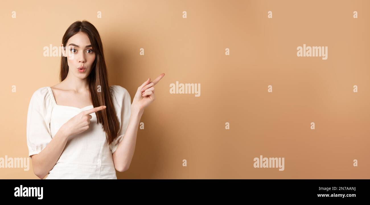 Wow look here. Impressed caucasian woman in white dress pointing ...