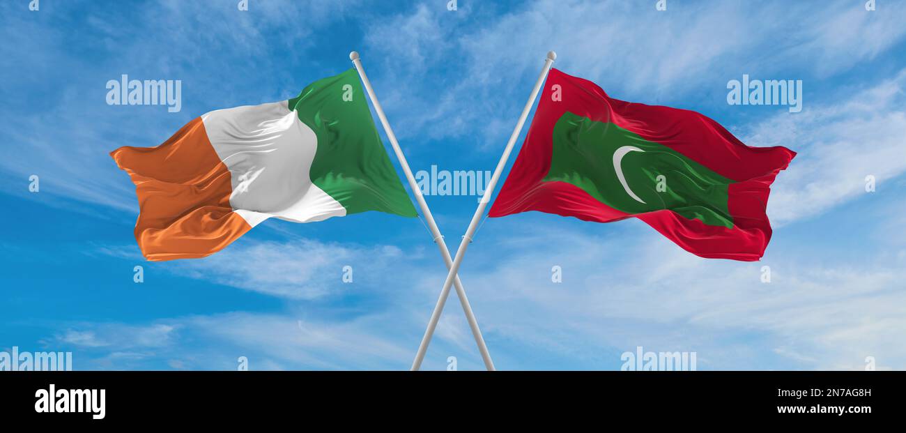 two crossed flags Maldives and Ireland waving in wind at cloudy sky ...