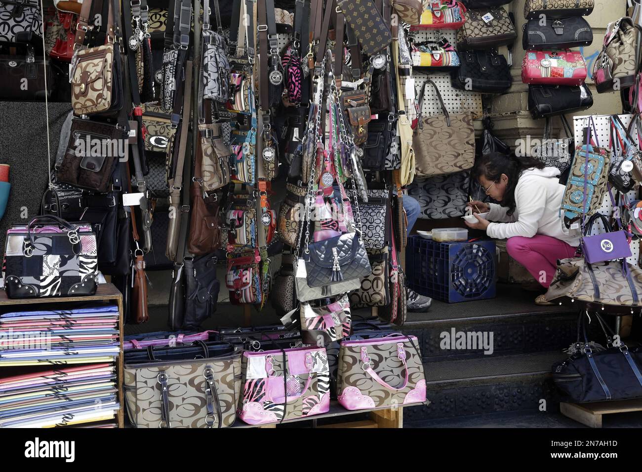 A woman eats among a display of purses for sale on Canal Street in New ...