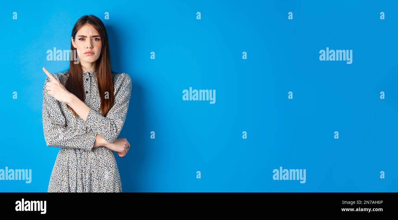 Disappointed frowning girl pointing left and looking displeased ...