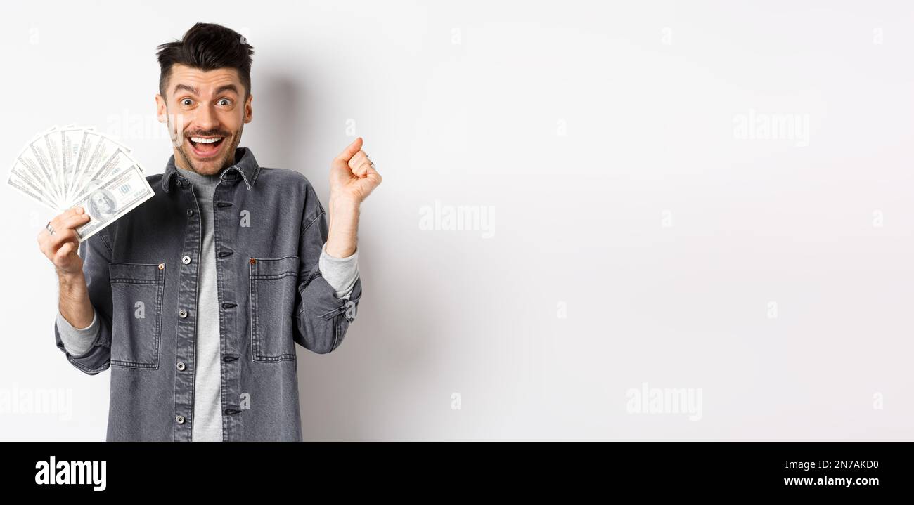 Cheerful young man jumping from excitement and showing dollar bills ...