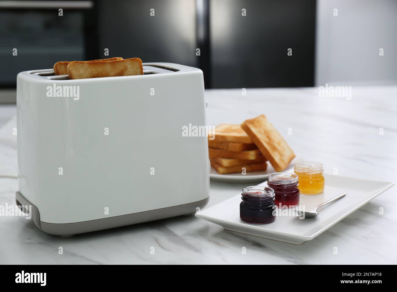 Modern toaster with slices of bread and different jams on white marble table in kitchen Stock ...