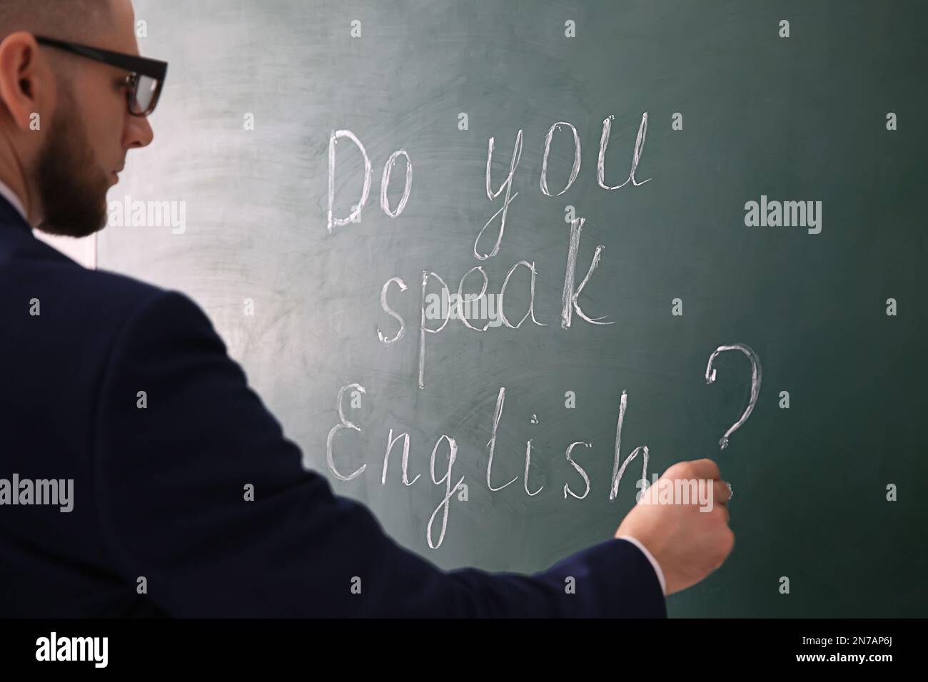 Teacher writing words Do You Speak English? on green chalkboard ...