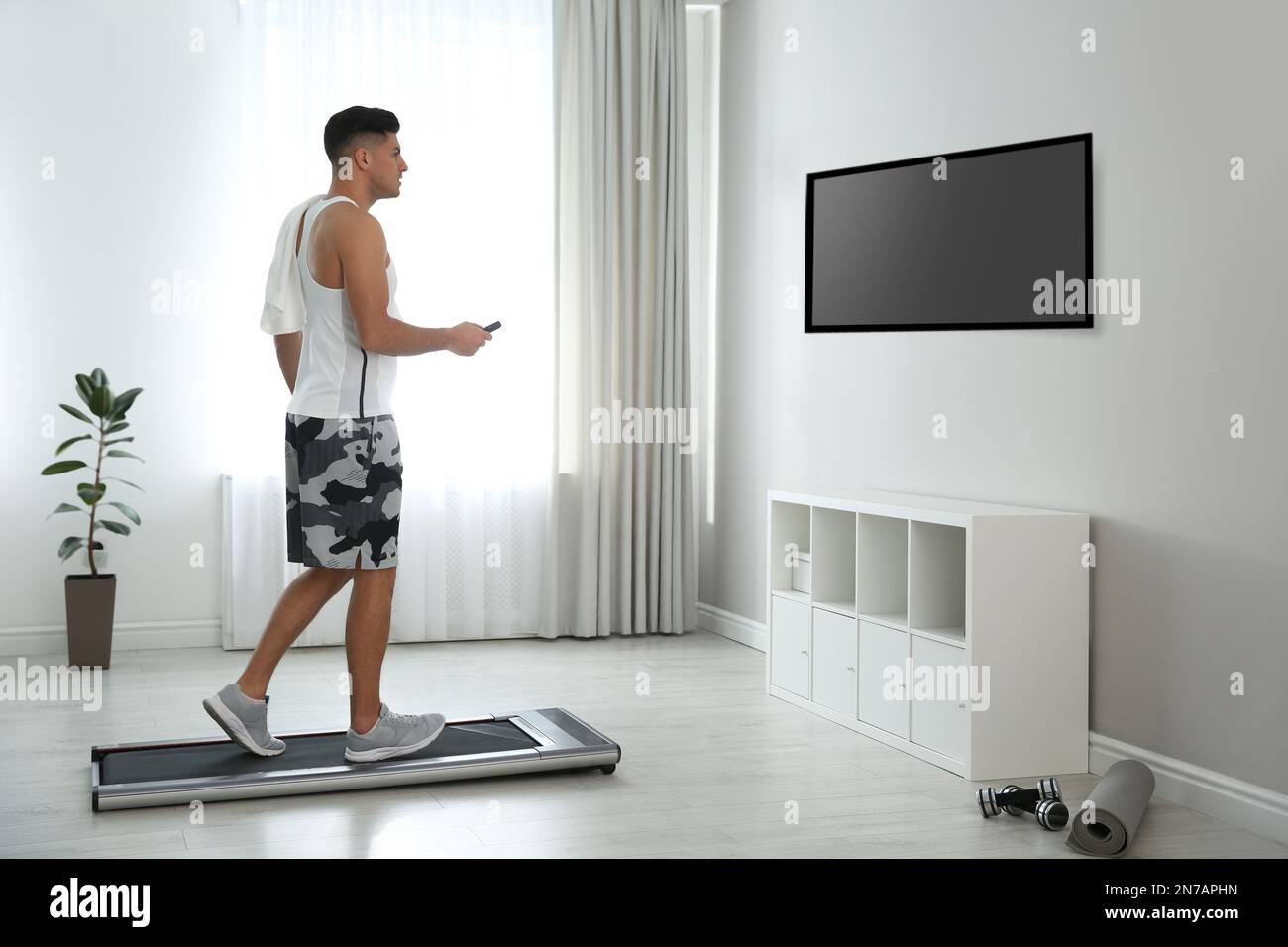 Sporty man training on walking treadmill while watching TV at home ...