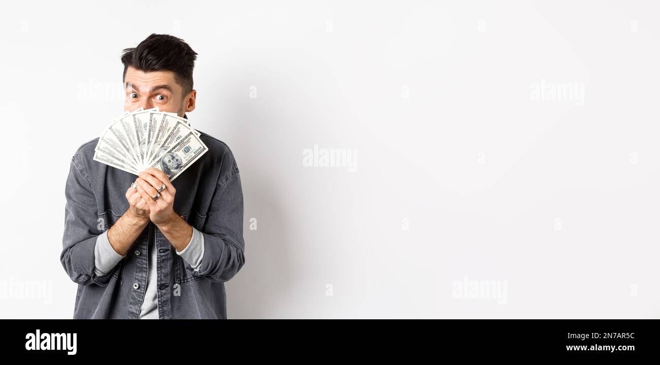 Excited funny guy hiding face behind dollar bills and smiling, showing ...