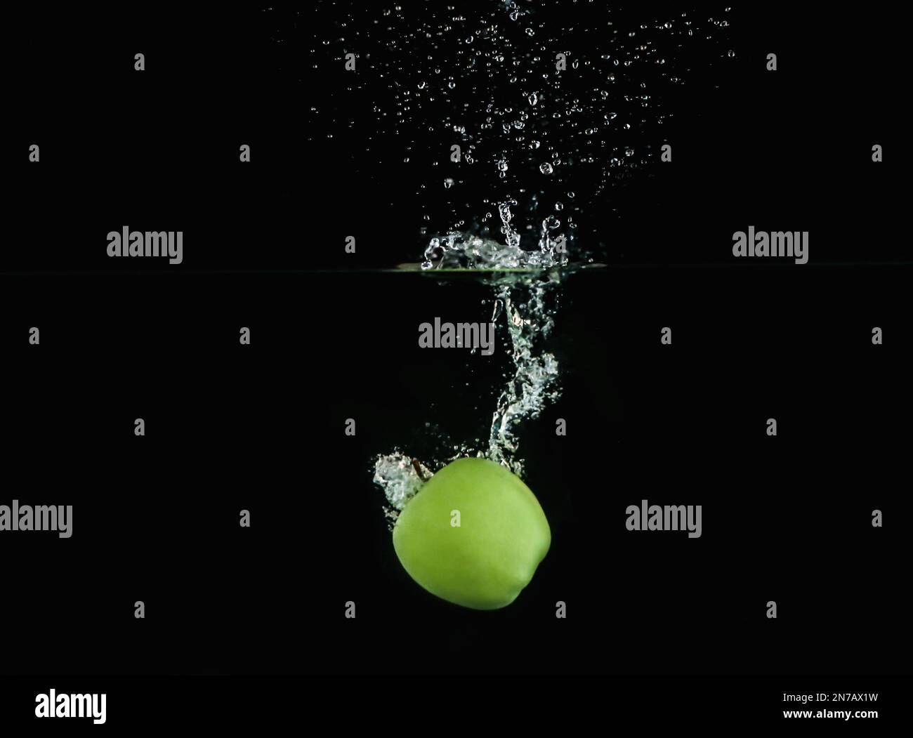 Ripe green apple falling down into clear water with splashes against ...