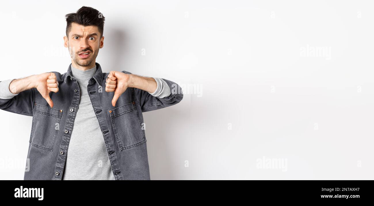 Disappointed guy showing thumbs down and frowning, looking skeptical at ...