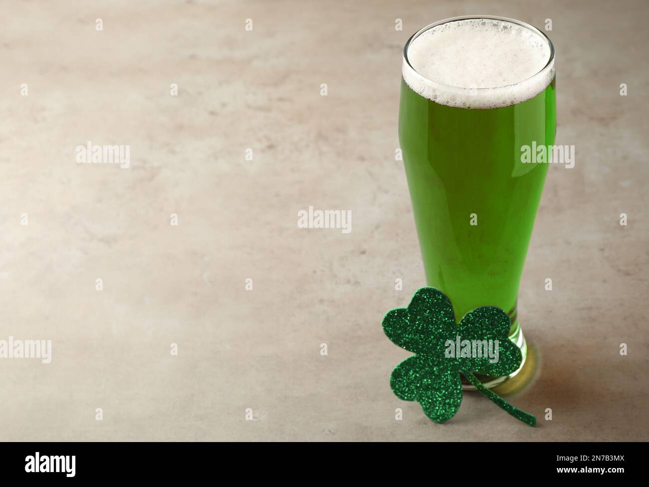 Glass of green beer with clover leaf on light grey table, space for ...