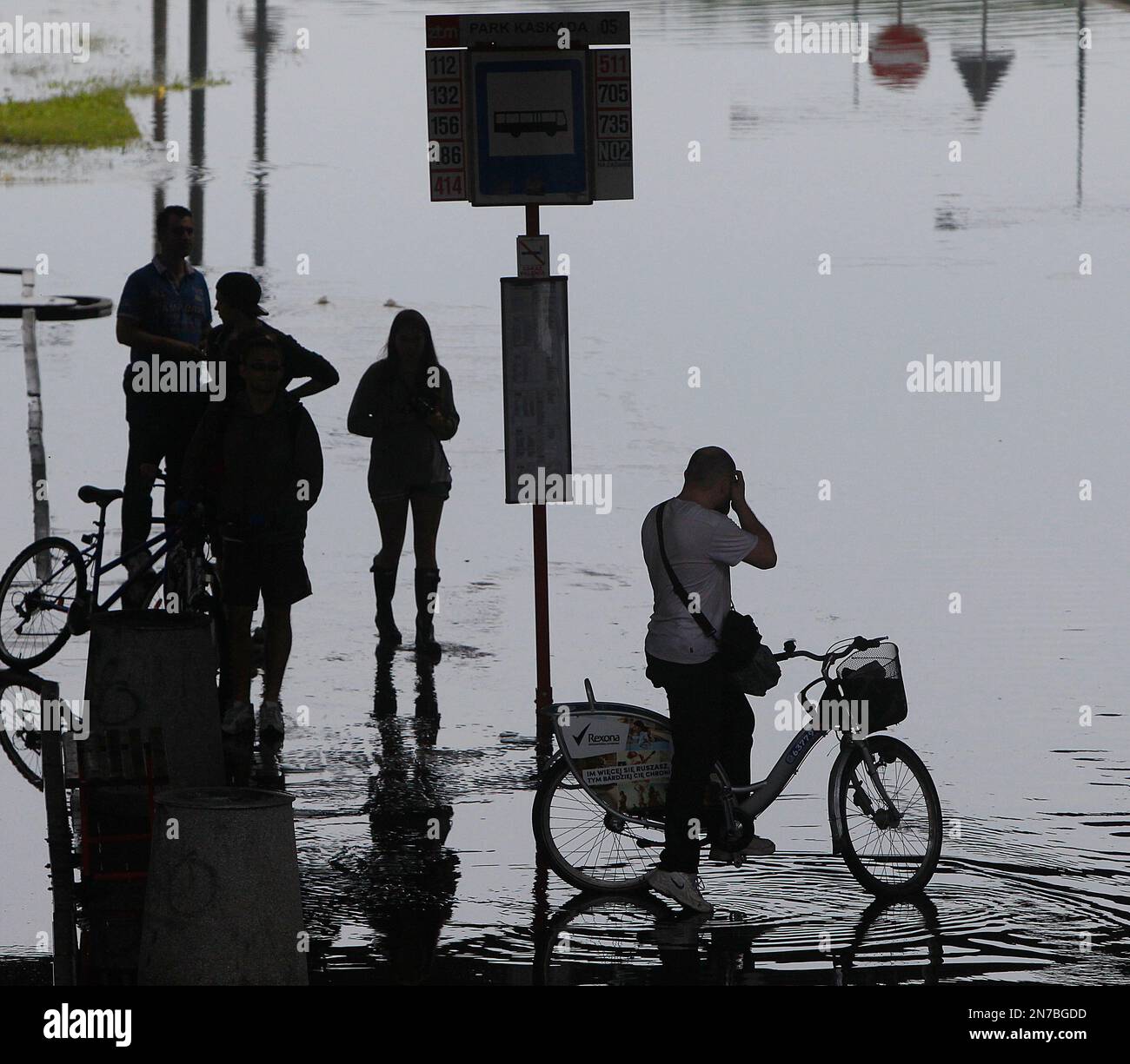 People look at a flooded street as heavy rain hits the town, in Warsaw ...