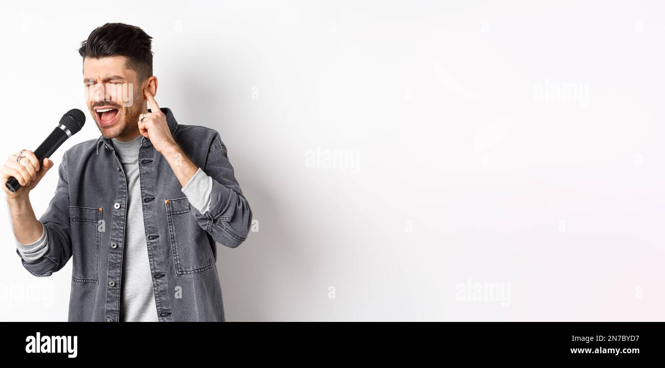 Handsome singer trying to reach high note, singing in microphone and ...