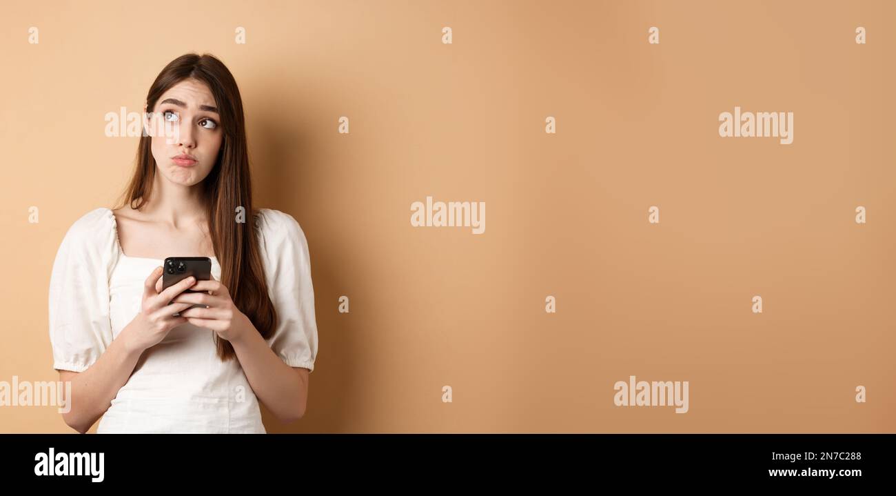 Confused young woman thinking after reading news on mobile phone ...