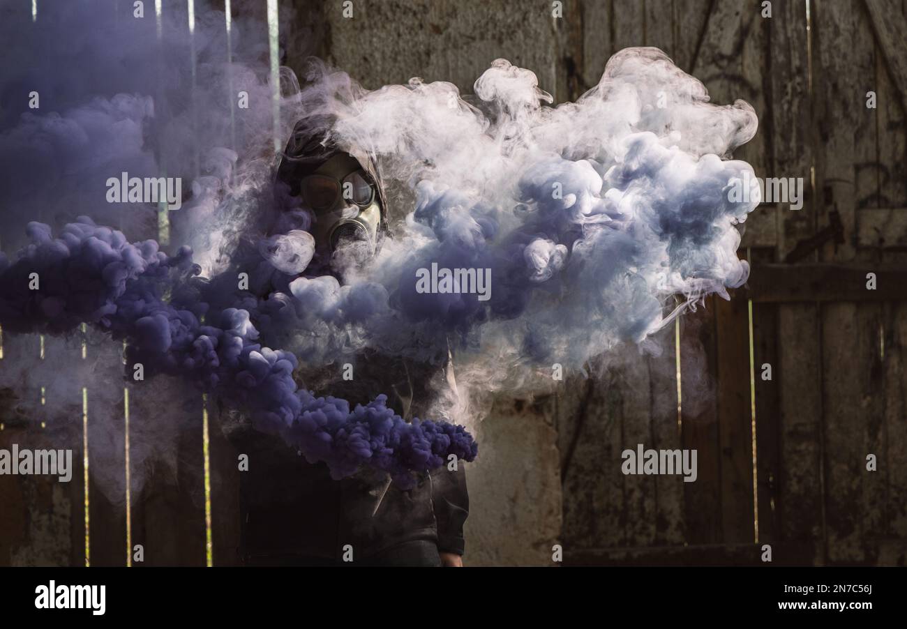 A man in gas mask holding a smoke bomb. Bright purple colorful smoke ...