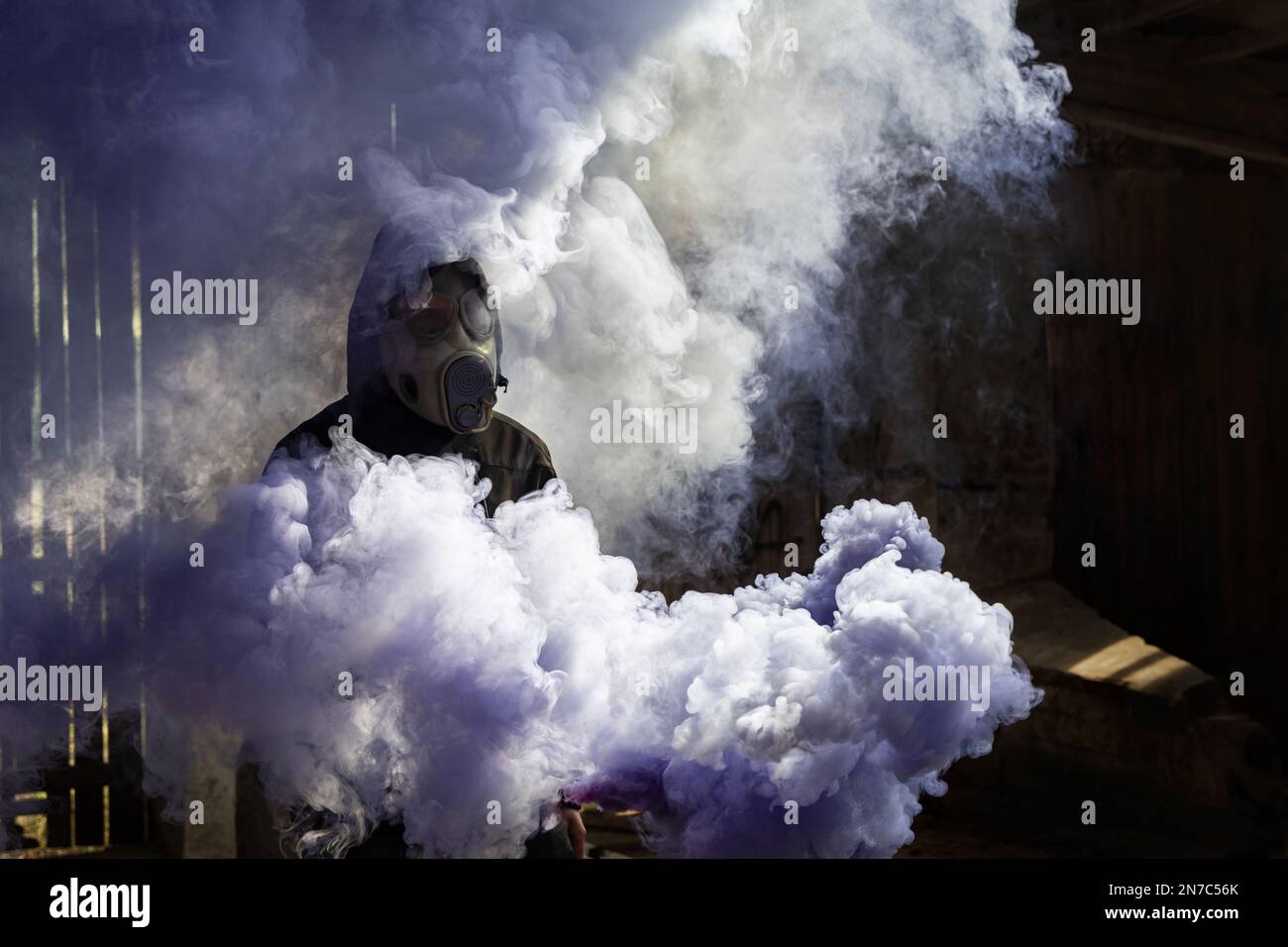 A man in gas mask holding a smoke bomb. Bright purple colorful smoke ...