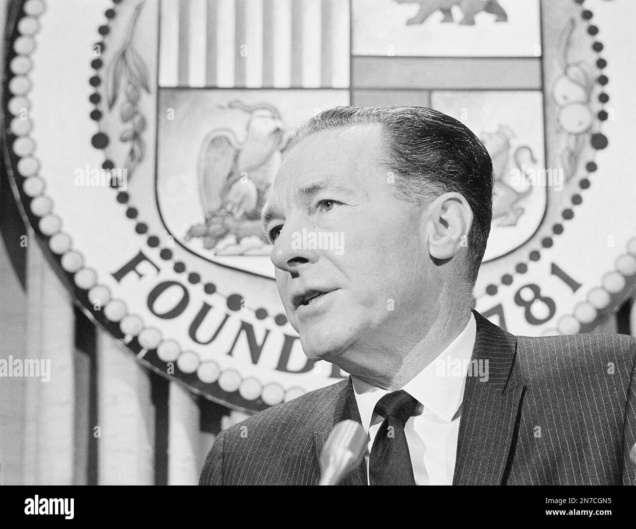 Mayor Sam Yorty of Los Angeles poses in his office in front of the seal ...