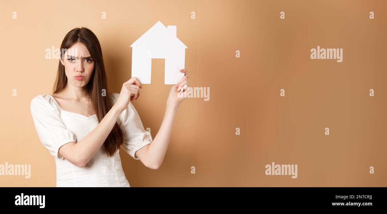 Real estate. Angry girl showing house cutout and frowning upset ...