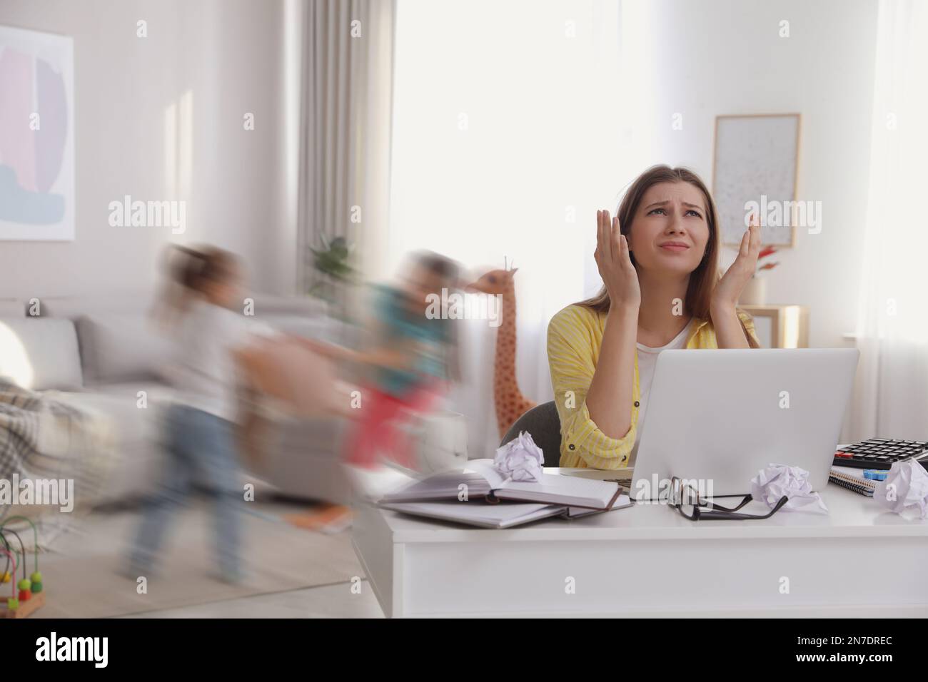 Children disturbing overwhelmed woman in living room. Working from home ...