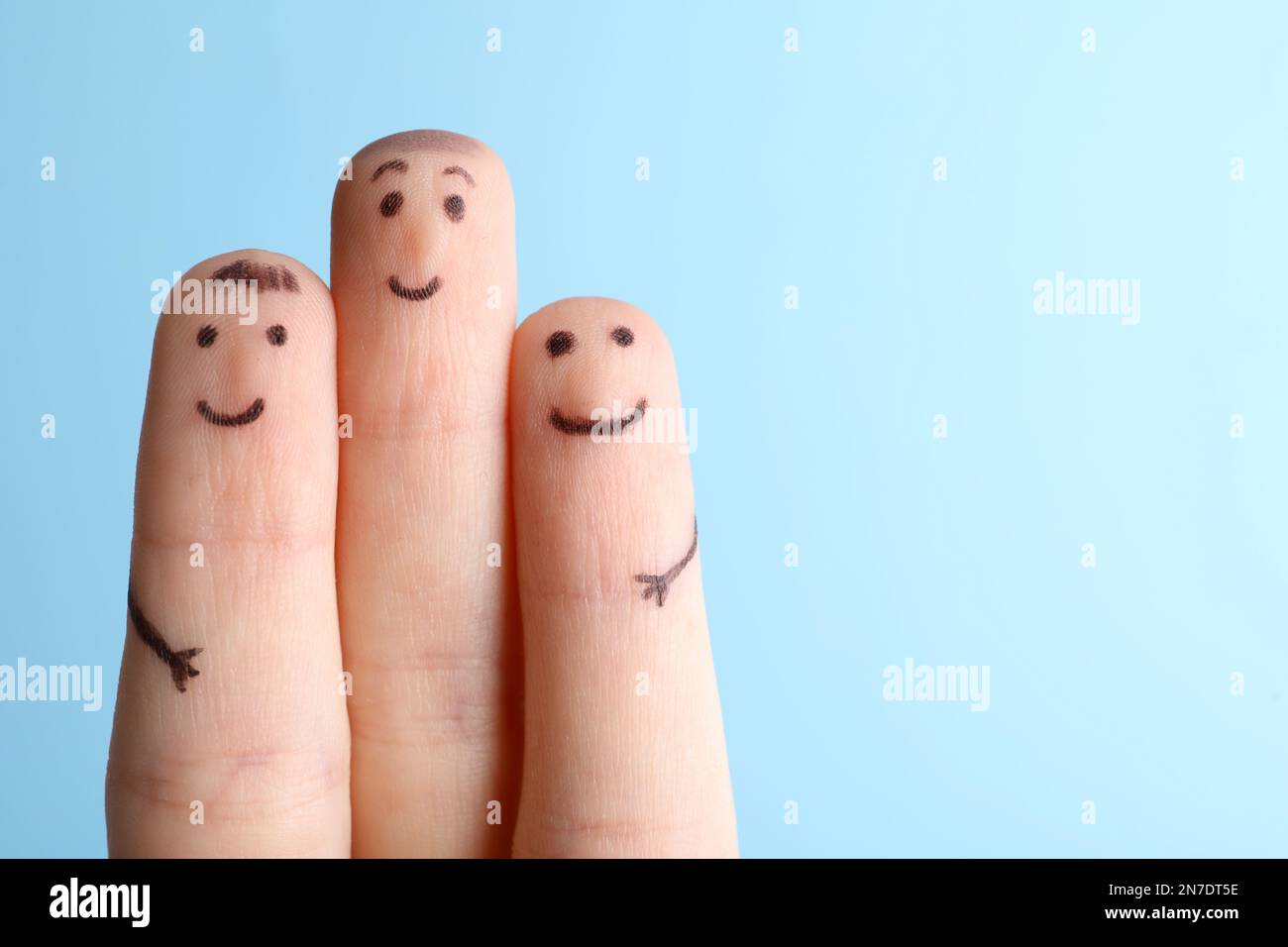 Three fingers with drawings of happy faces on light blue background ...