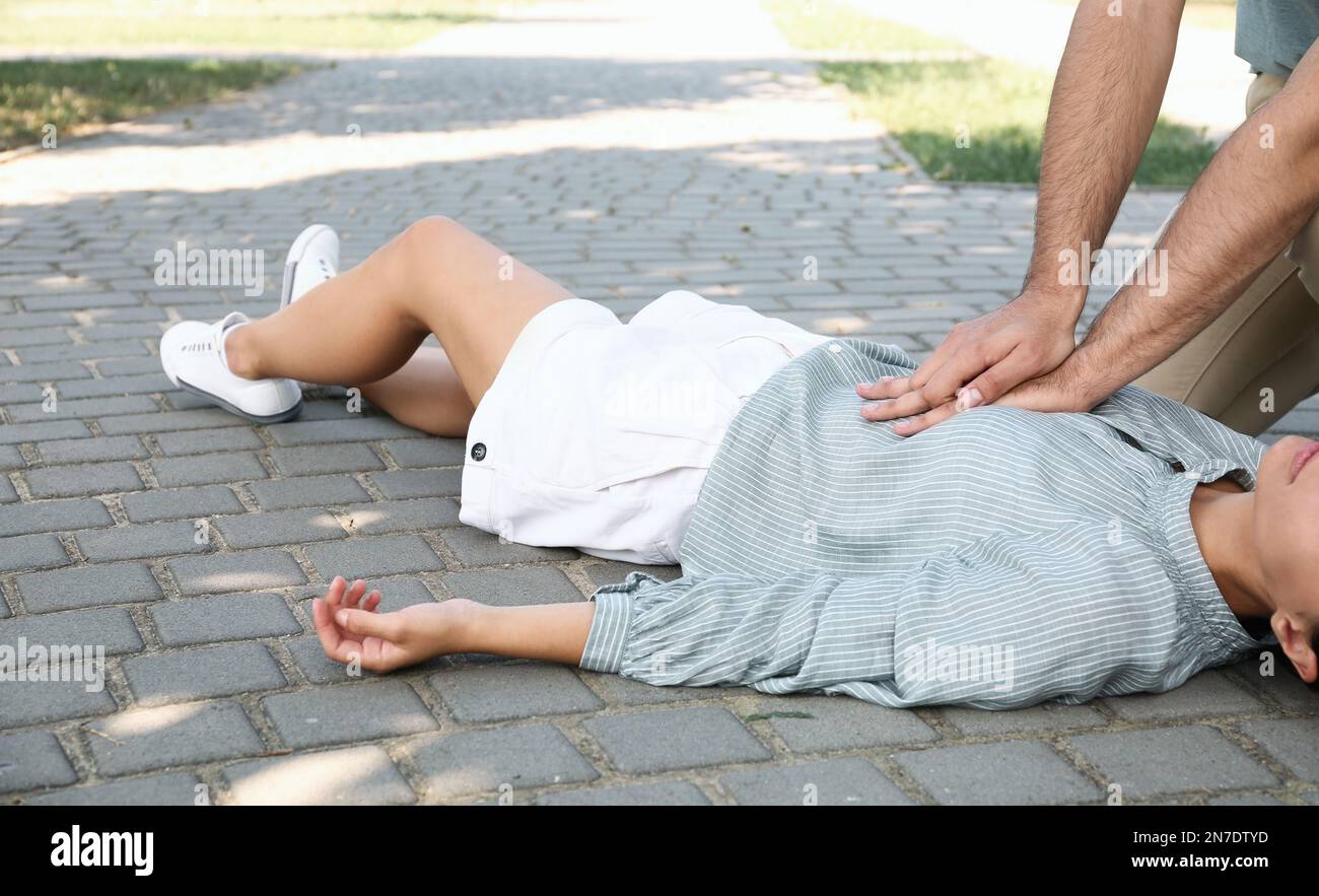 Young man performing CPR on unconscious woman outdoors, closeup. First ...