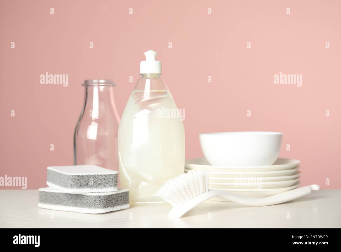 Cleaning supplies for dish washing and plates on white table against ...