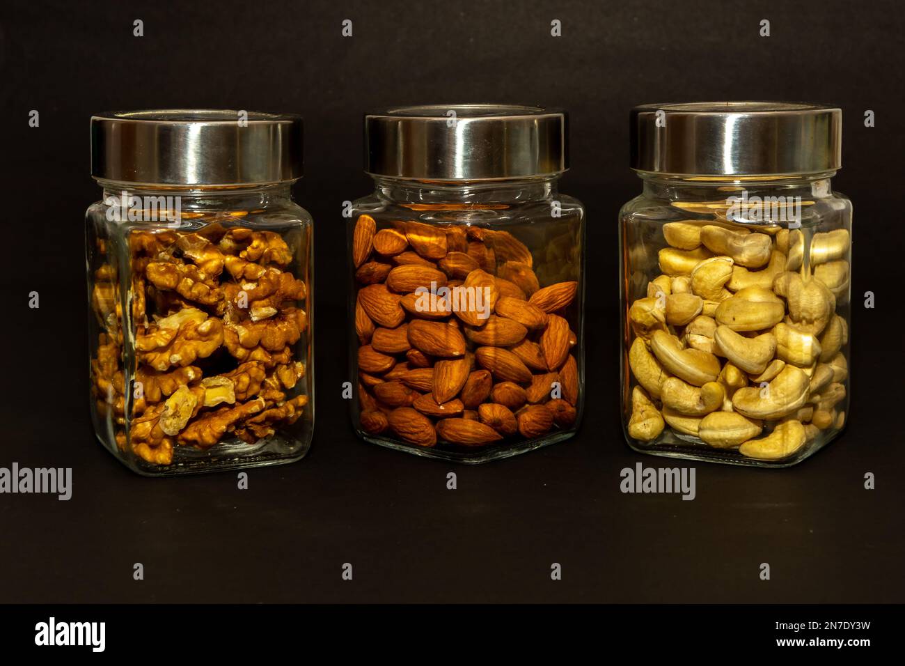 Glass jars filled with varieties of dry fruits against black background ...