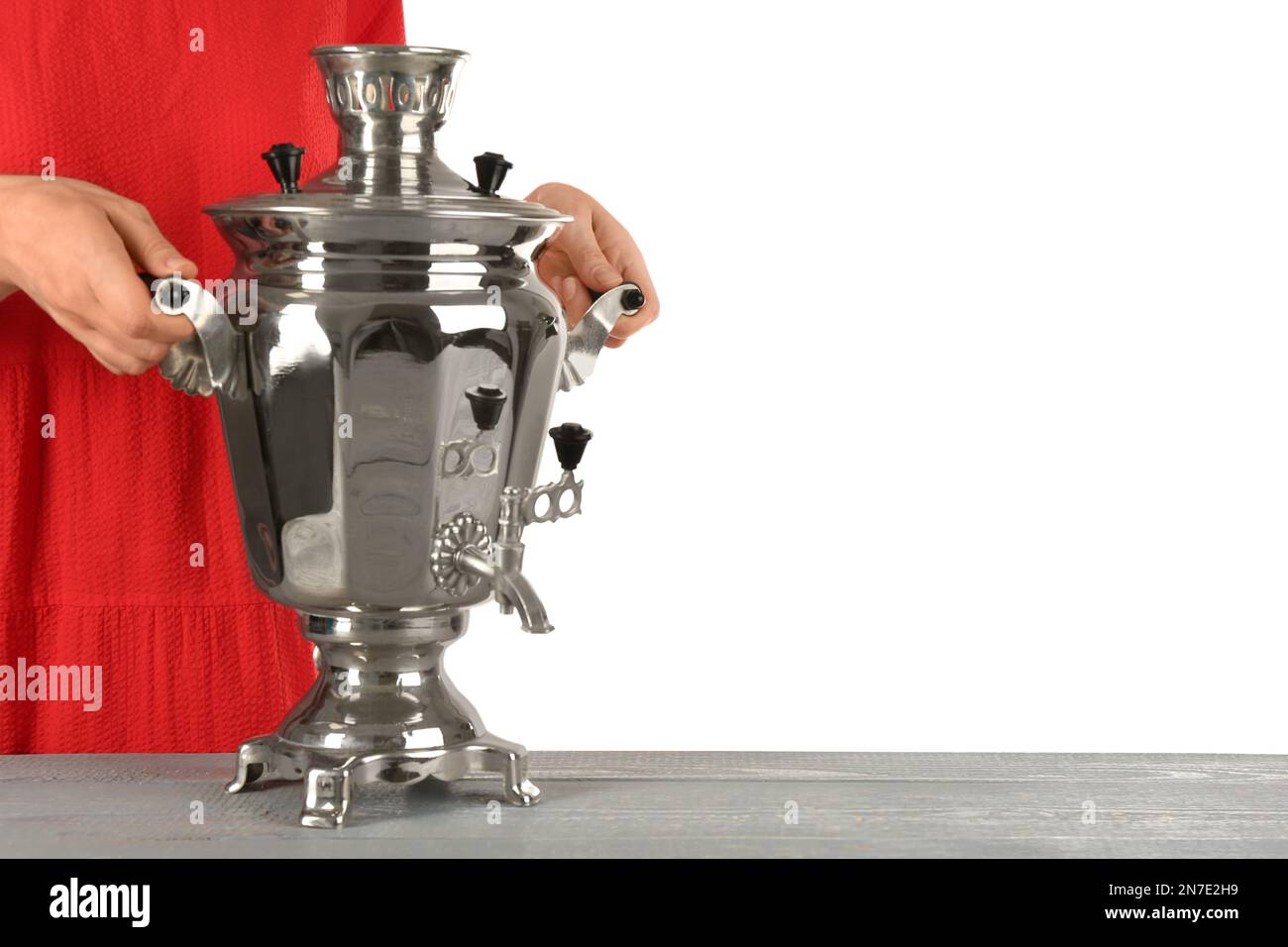 Woman holding traditional Russian samovar on grey table against white ...