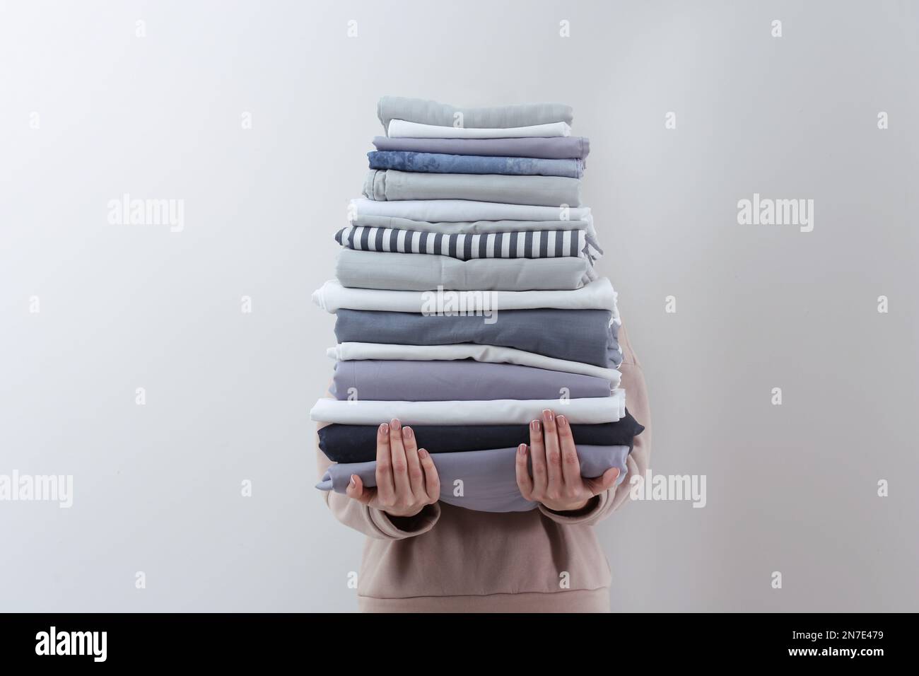 Woman holding stack of clean bed linens on light grey background Stock ...