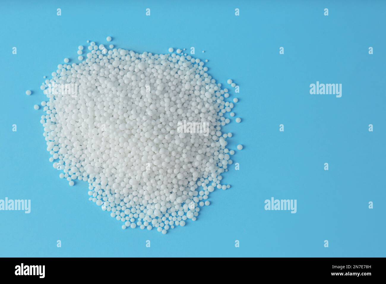 Pellets of ammonium nitrate on light blue background, flat lay with space for text. Mineral ...