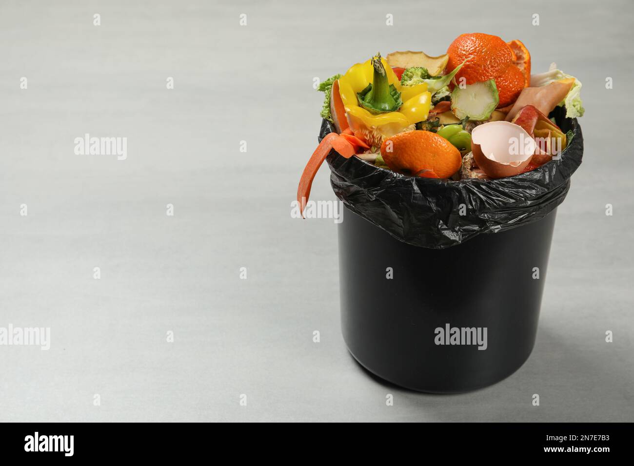 Trash bin with natural garbage on light background, space for text ...