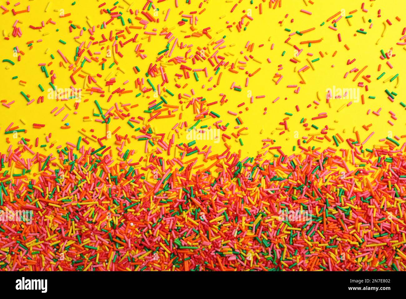 Bright colorful sprinkles on yellow background, flat lay. Confectionery ...