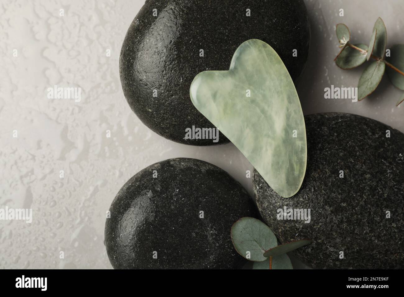 Jade gua sha tool, spa stones and eucalyptus branches on grey table ...