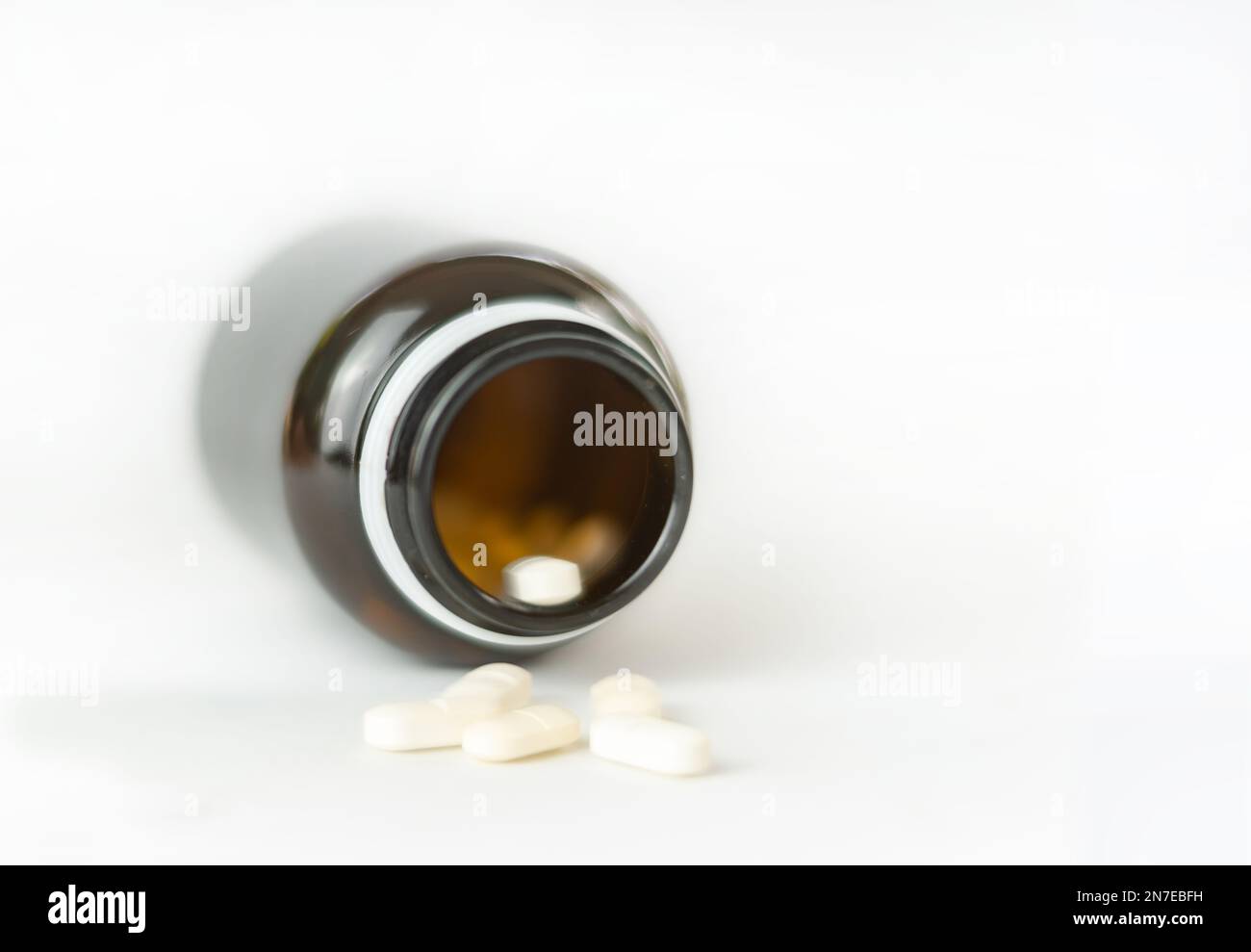 White medical pills and tablets spilling out of a drug bottle on ...