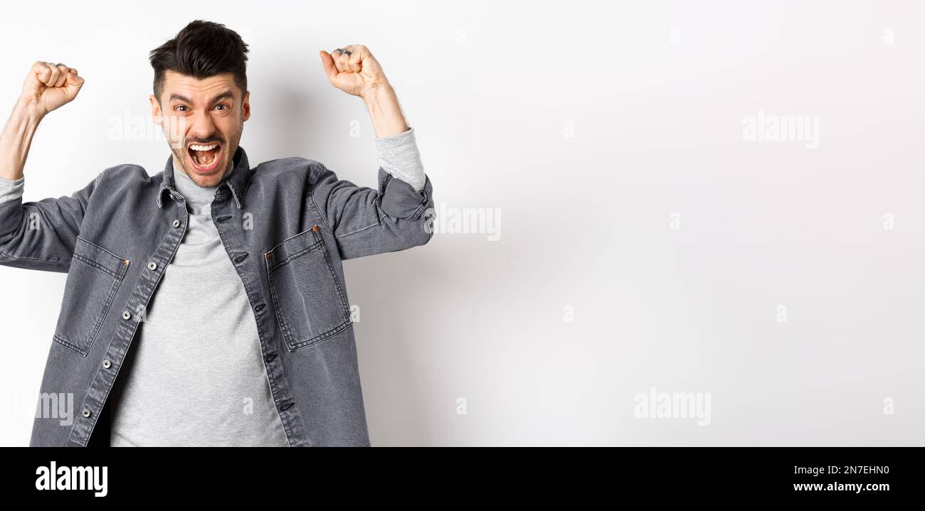 Motivated young man shouting and raising hands up, watching sports game ...