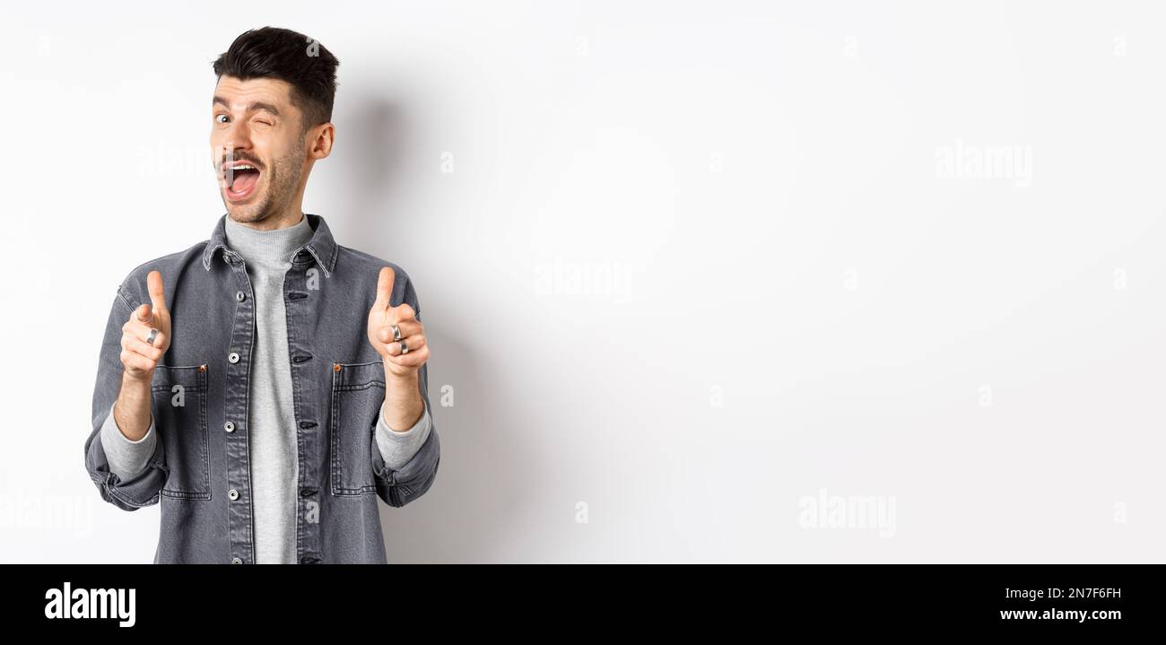Funny handsome guy winking and pointing fingers at camera, inviting you ...