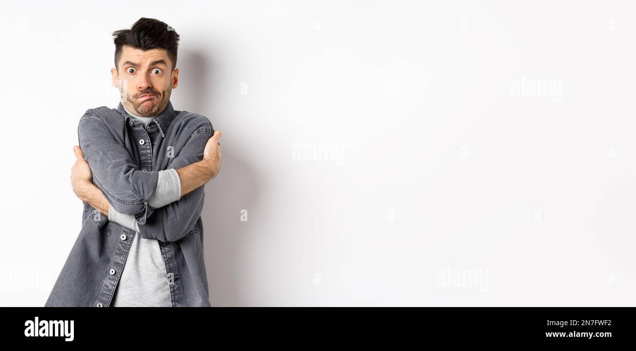 Funny young man hugging himself and grimacing, feeling embarrassed and ...