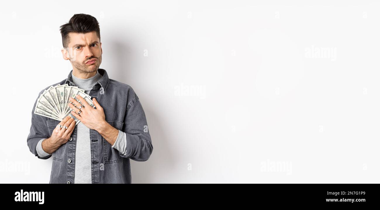 Greedy guy frowning and hugging dollar bills, unwilling to share money ...