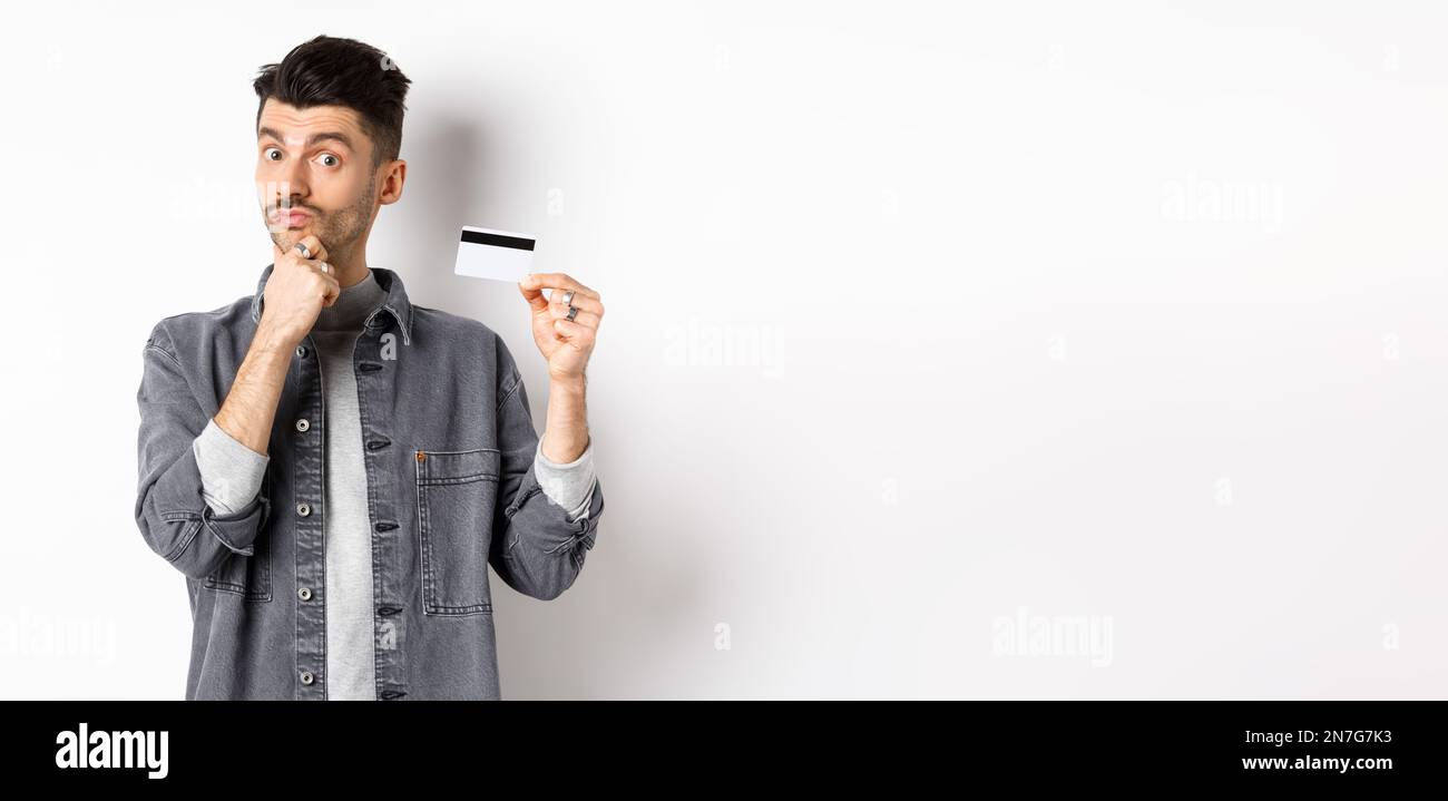 Thoughtful guy holding plastic credit card and thinking, looking ...