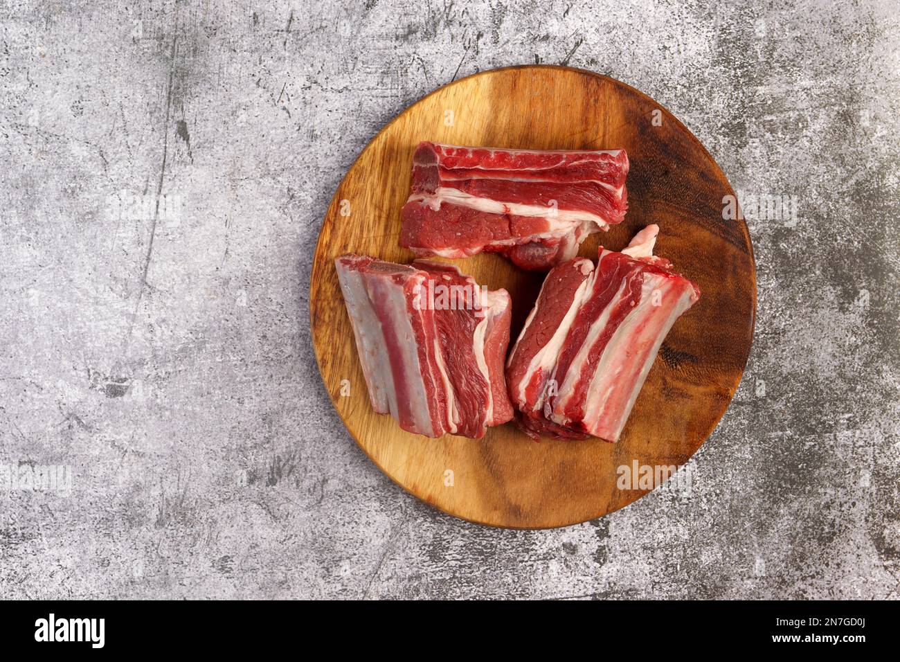 Raw beef ribs on a cutting wooden board on a dark grey background. Top ...