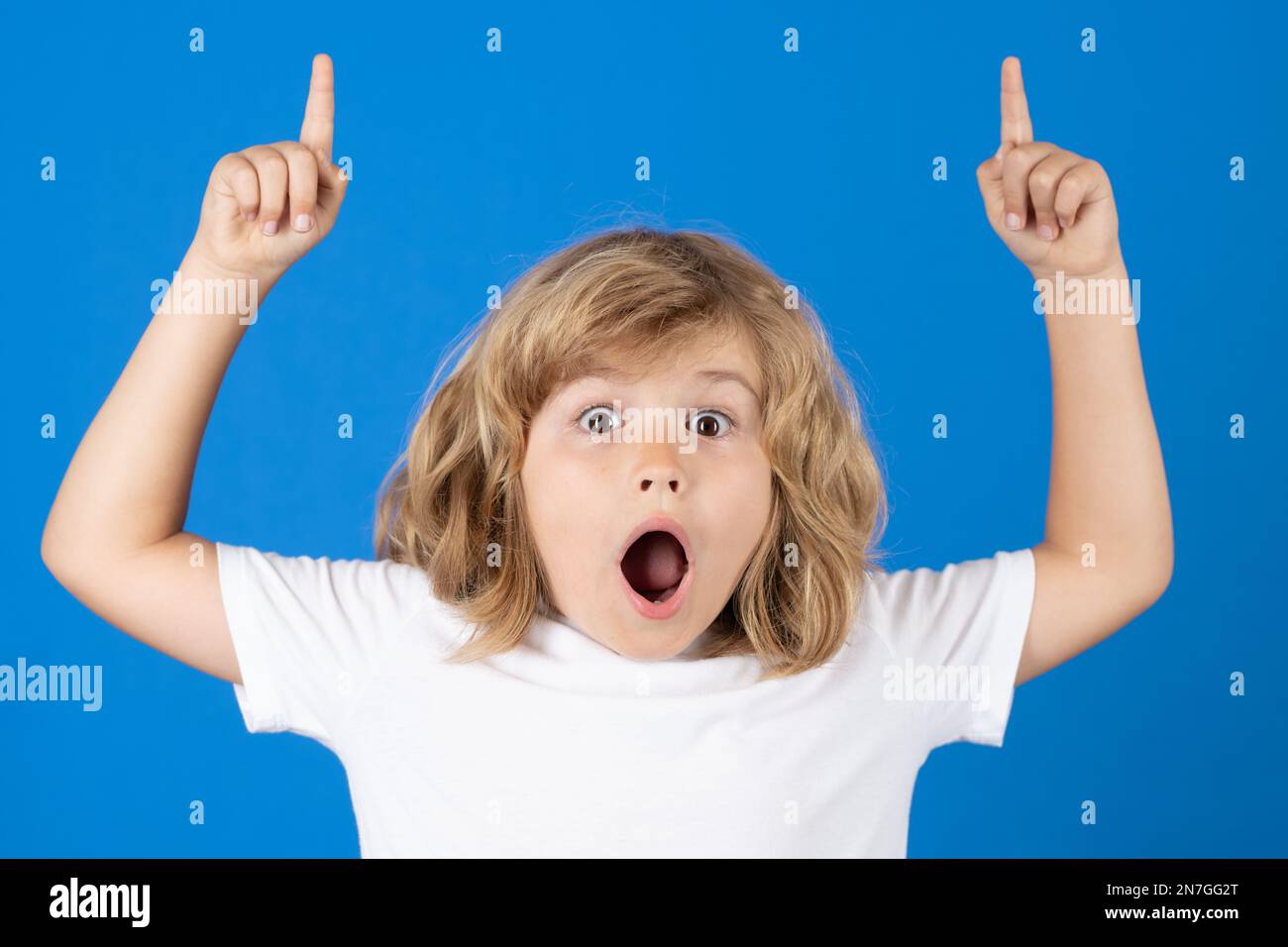 Surprised kid pointing up finger on blue studio background. Shocked kid ...