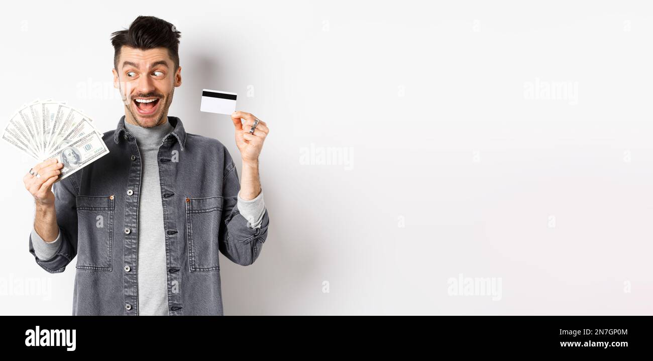 Excited guy holding plastic credit card and dollar bills, standing ...