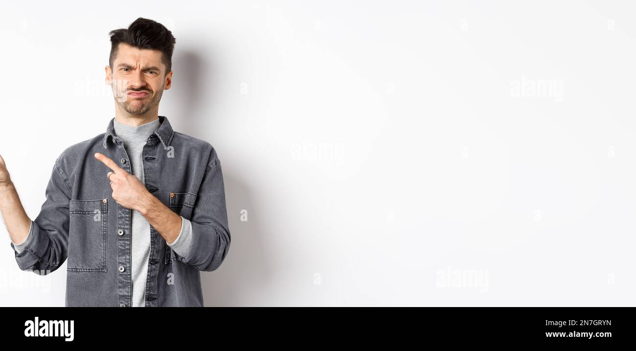 Skeptical and disappointed young man pointing fingers left, grimacing ...