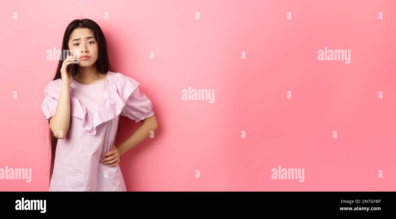 Sad asian girl calling someone, holding phone and talking, standing ...