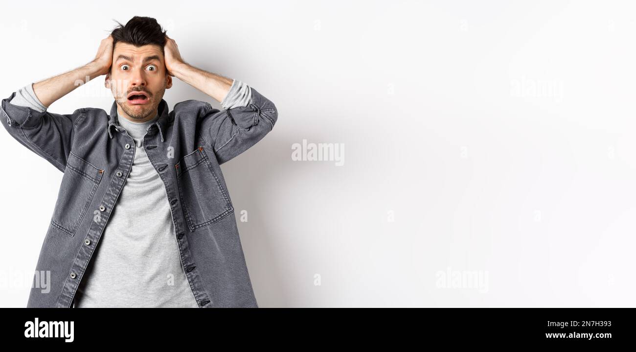 Alarmed young man grab head and pop eyes at camera, looking worried and ...