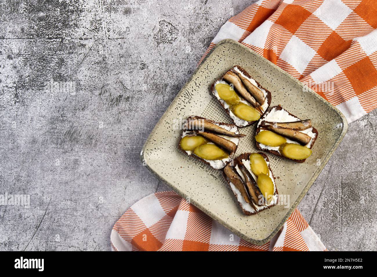 Sandwiches with sprats, curd cheese and pickles on a square plate on a ...