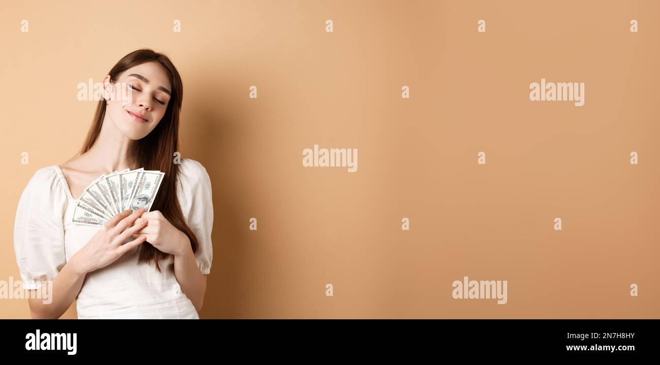 Stylish girl hugging money with pleased smile and closed eyes, like ...