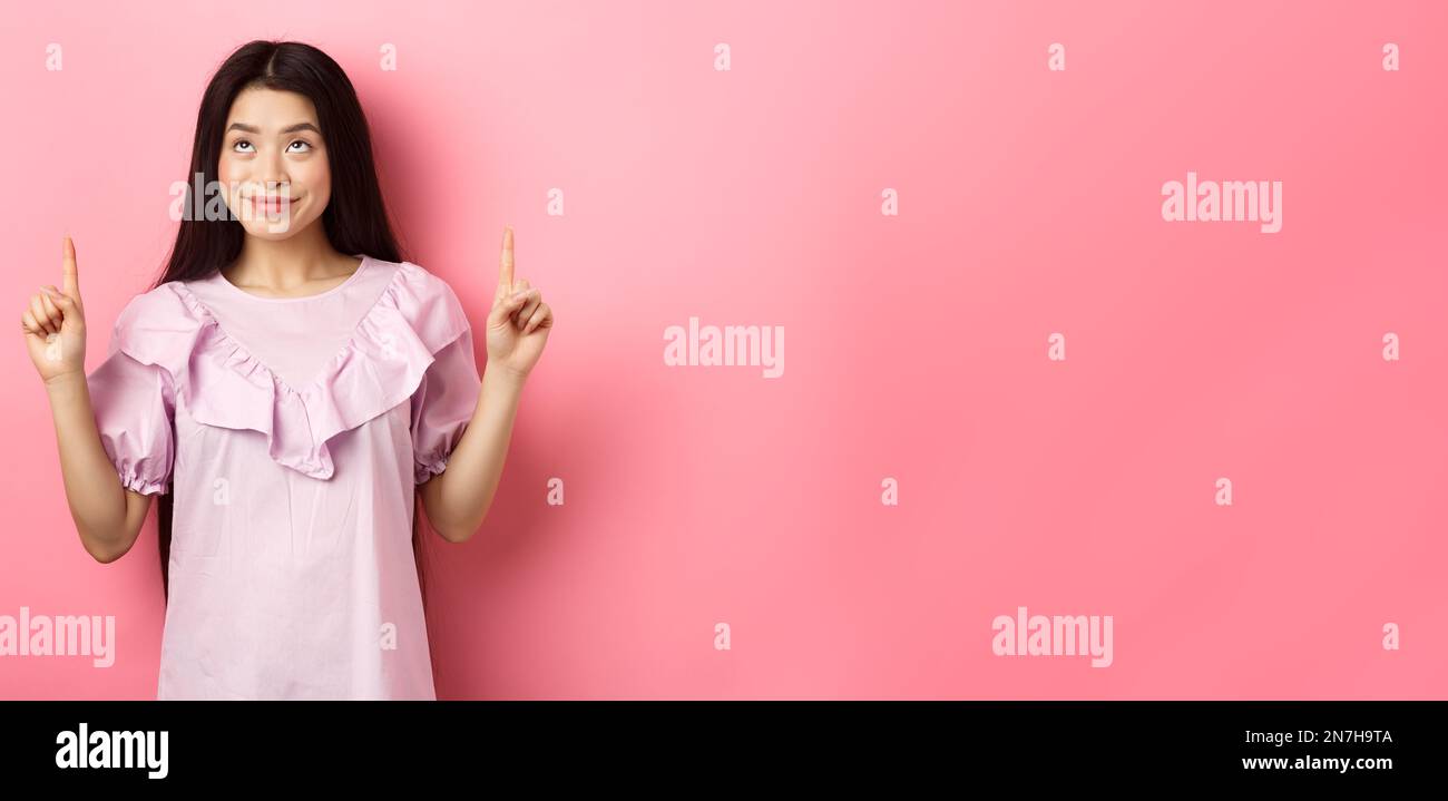 Beautiful smiling asian teen girl pointing fingers up, looking at ...