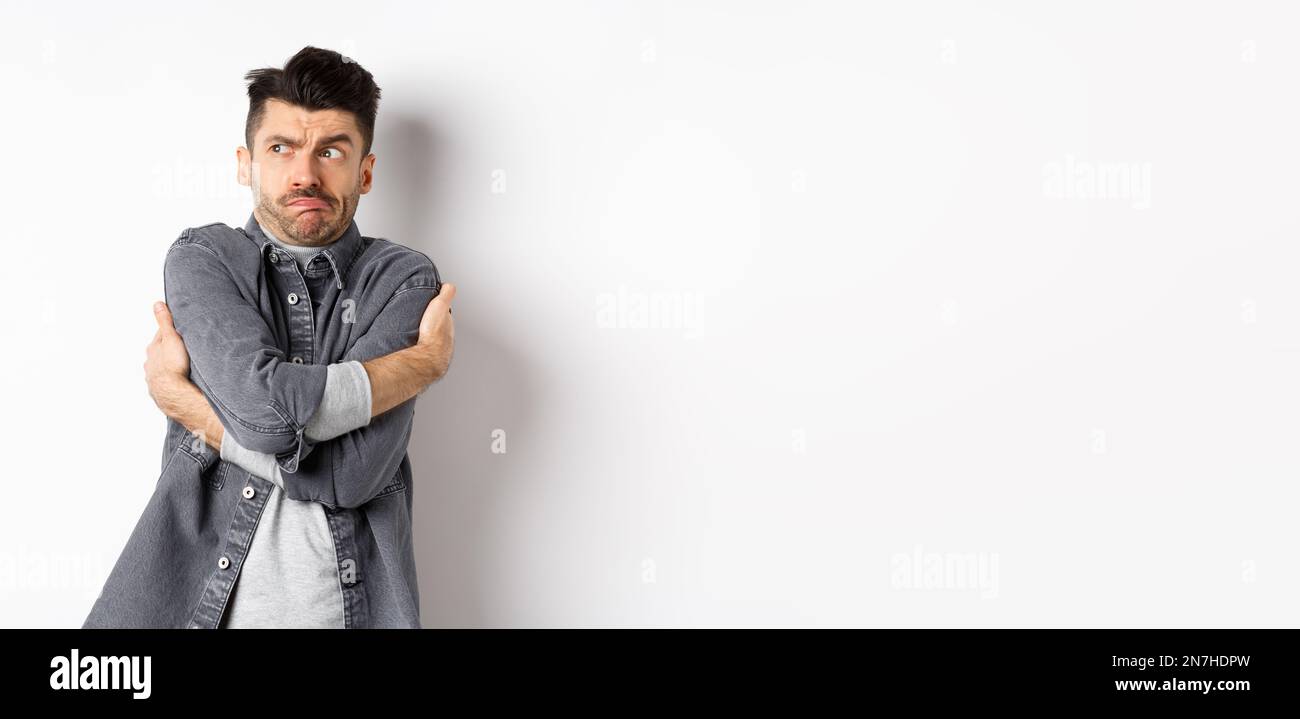 Displeased young man feeling discomfort, hugging himself and staring ...