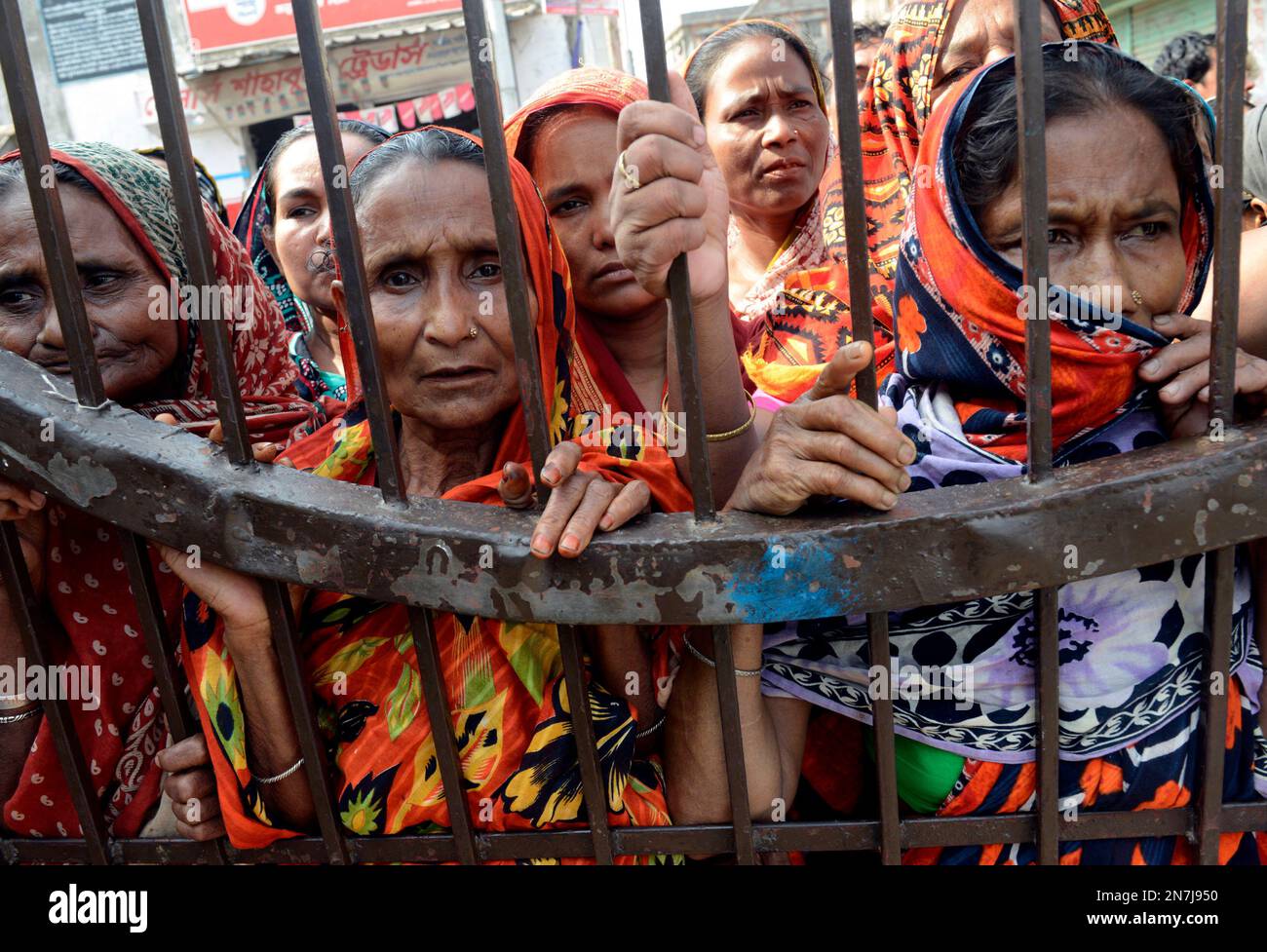 Women watch from behind a gate while unclaimed bodies are brought to a cemetery from the garment ...