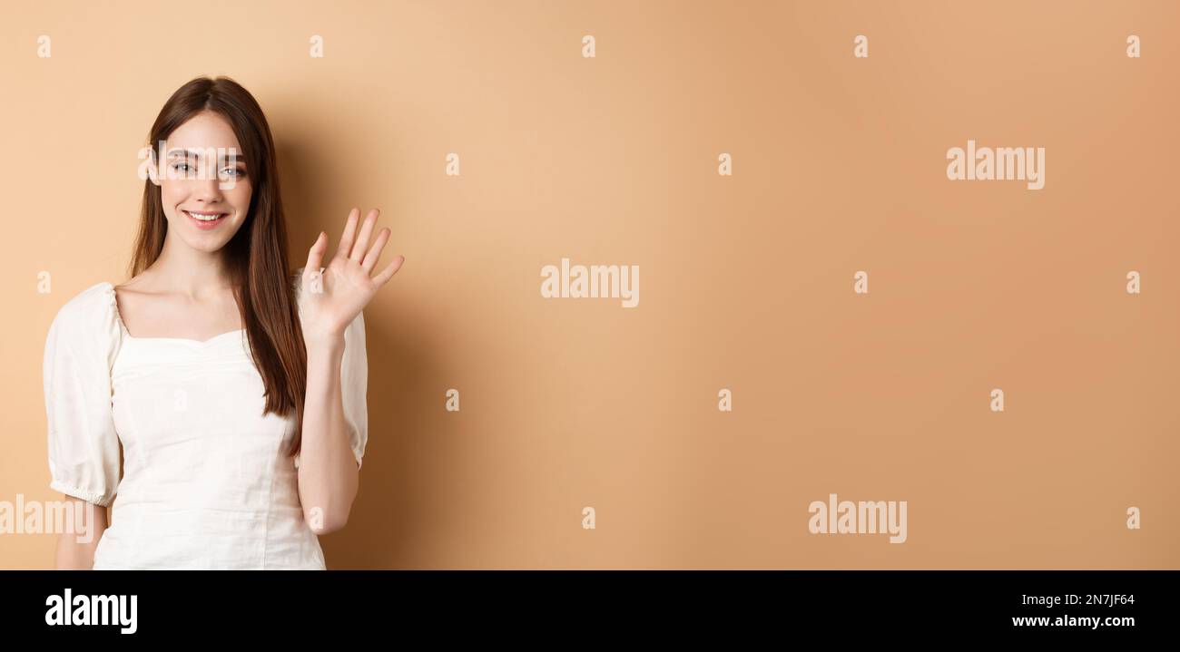 Friendly smiling woman say hello, waiving hand to greet you, standing ...