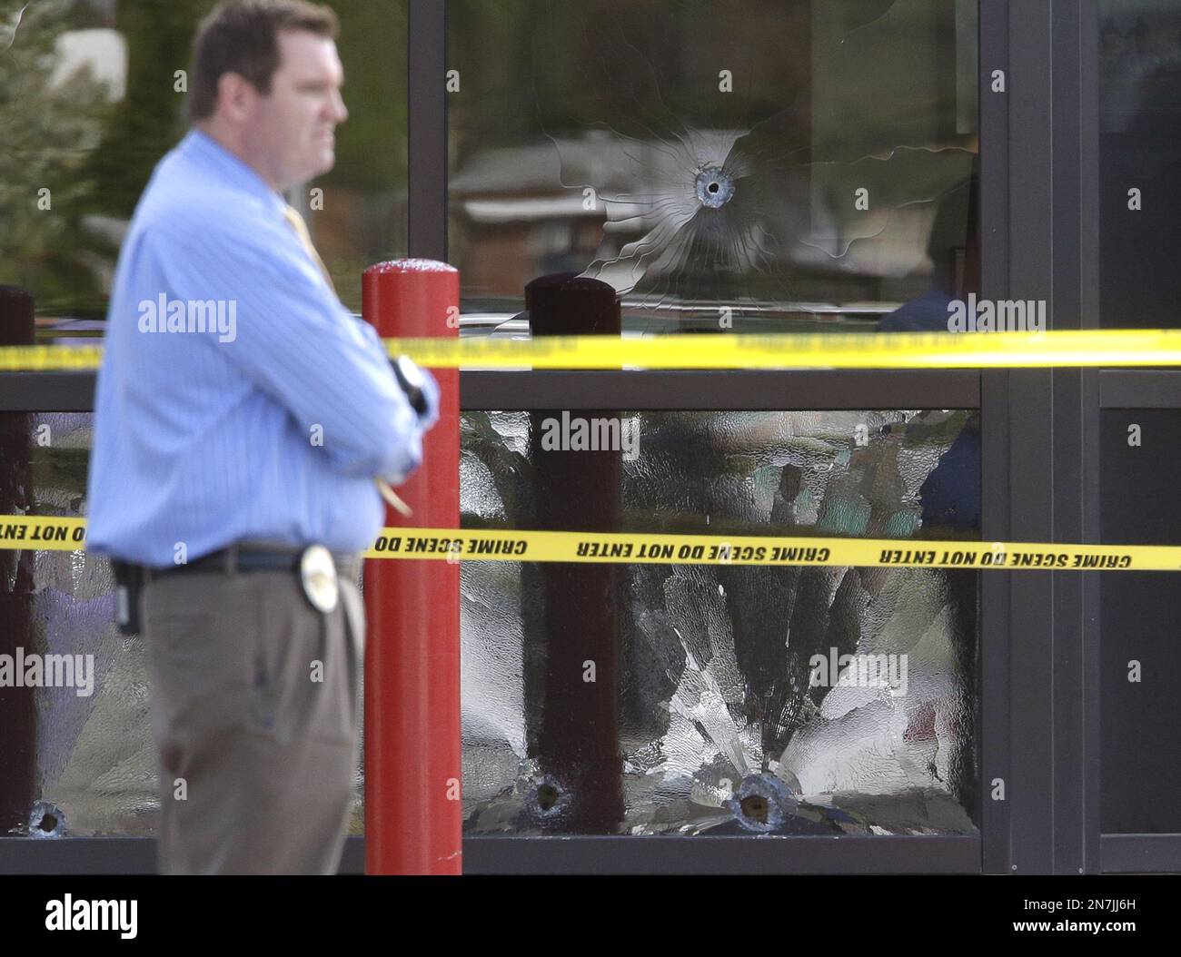 A West Valley City Police Officer stands near a bullet shattered window ...